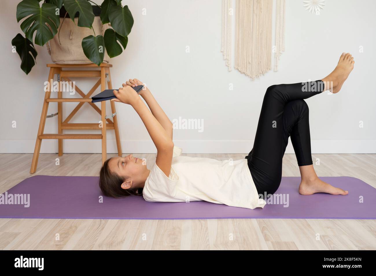 Girl watching yoga tutorial over tablet PC lying on exercise mat at ...