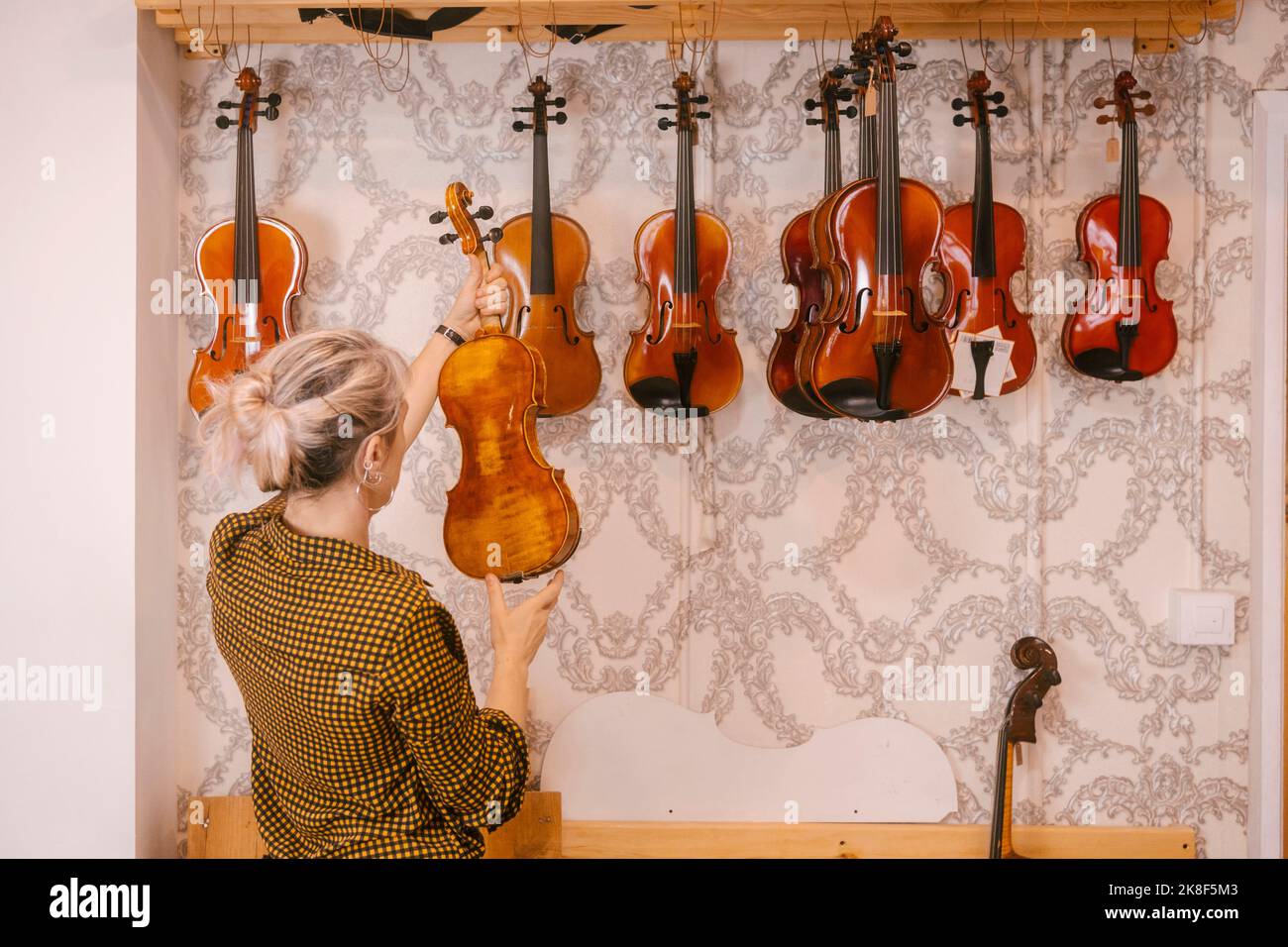 Luthier examining violins hanging at store Stock Photo - Alamy