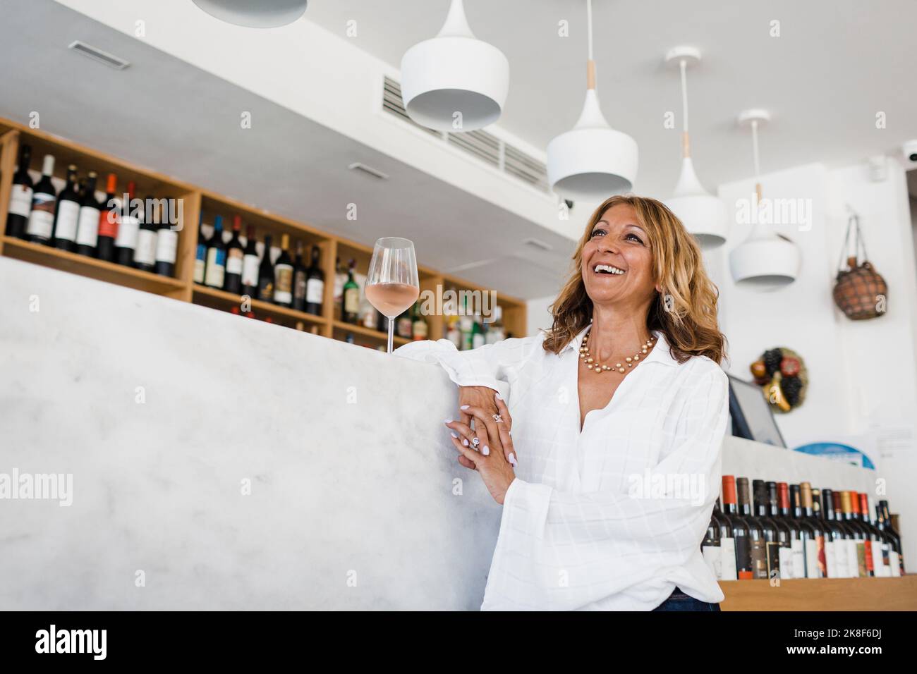 Happy mature restaurant owner with hands clasped standing by bar ...