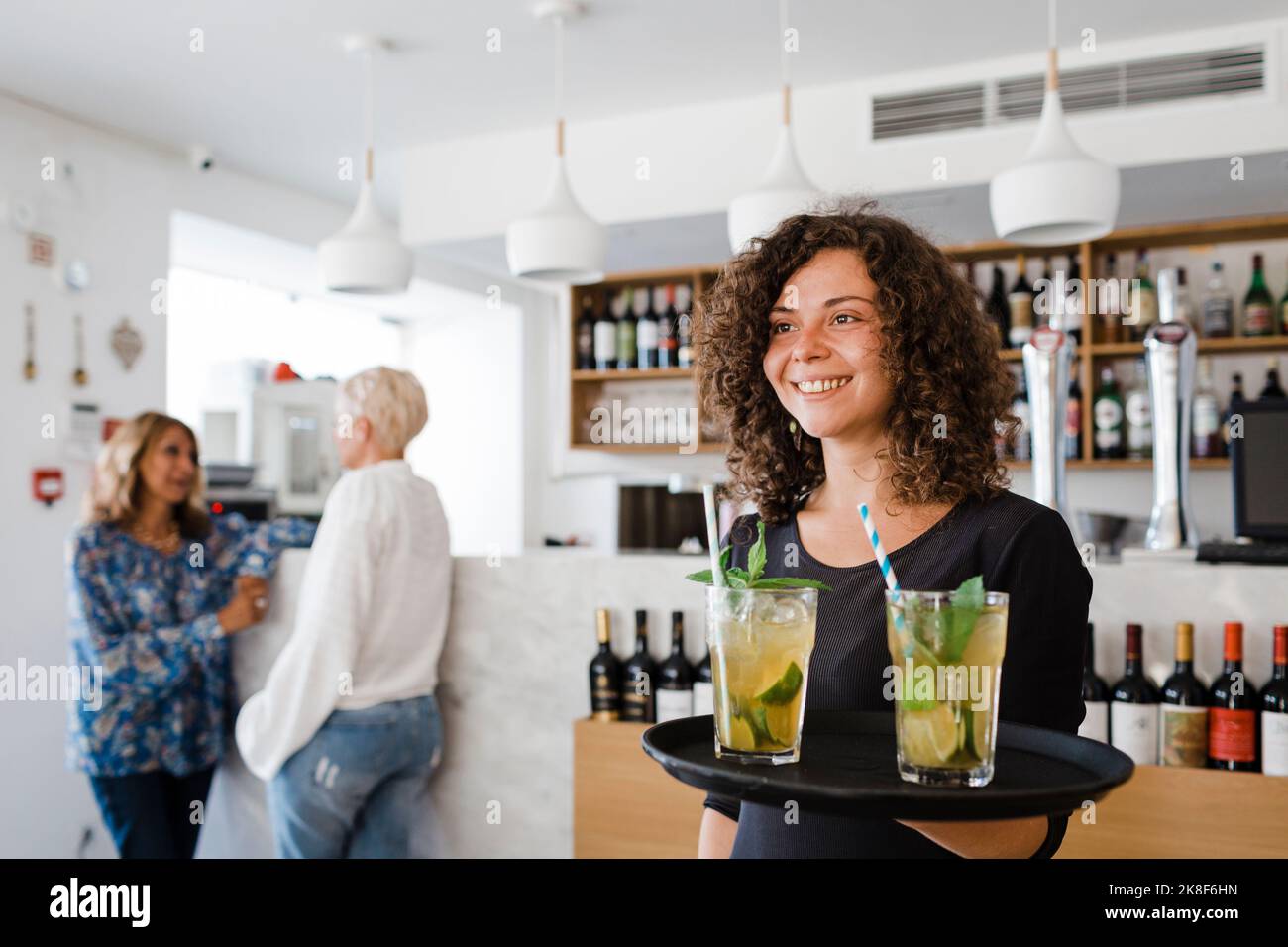 Happy young waitress with tray serving cocktail drinks at restaurant ...