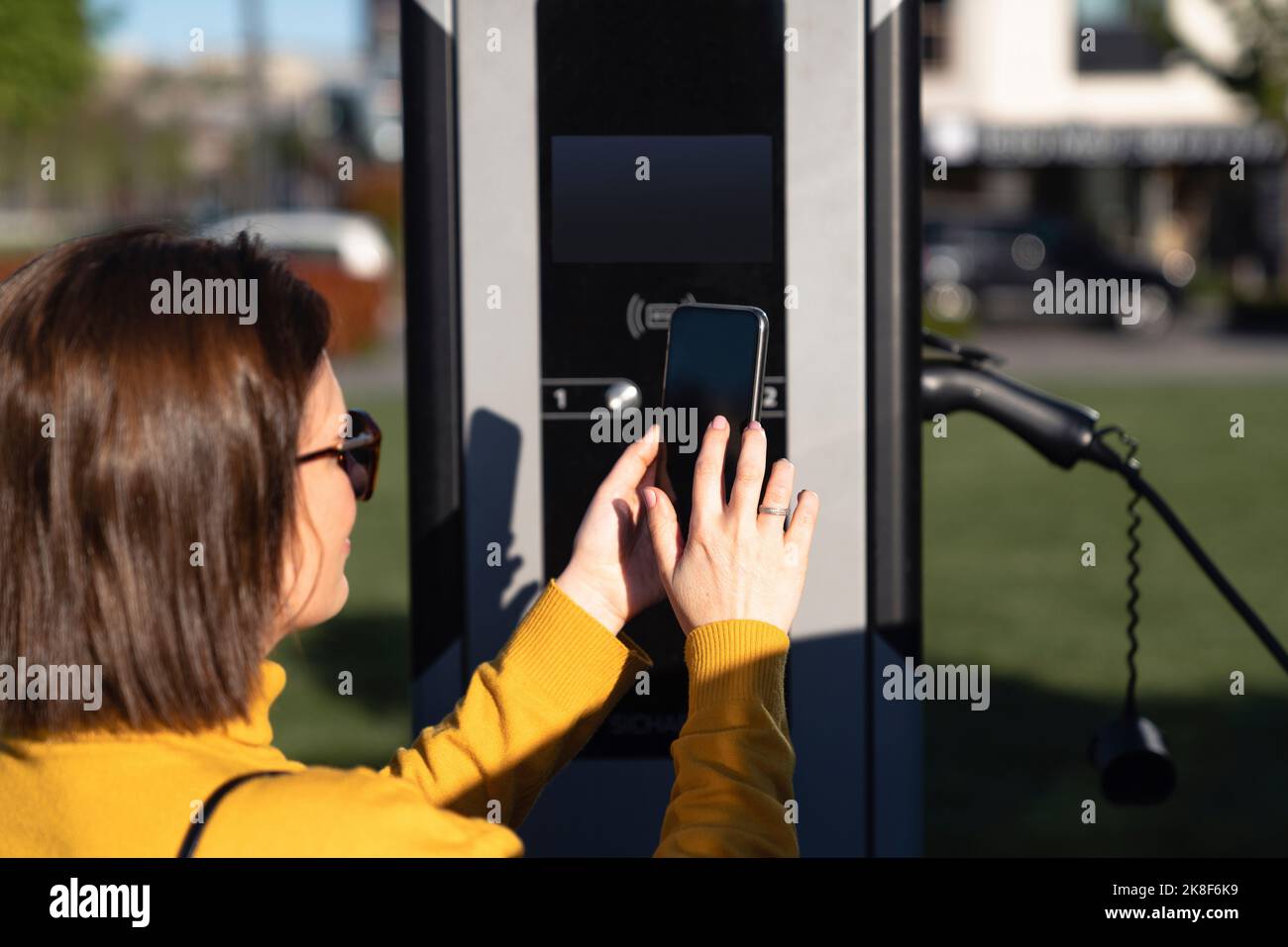 Woman making payment through smart phone at vehicle charging station ...