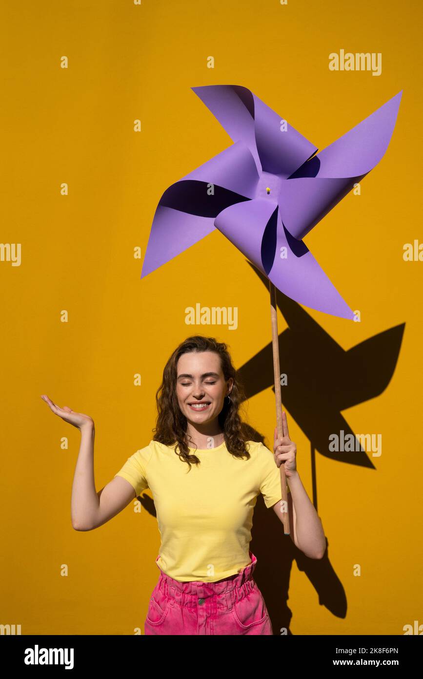Smiling woman with eyes closed holding pinwheel toy in front of yellow ...