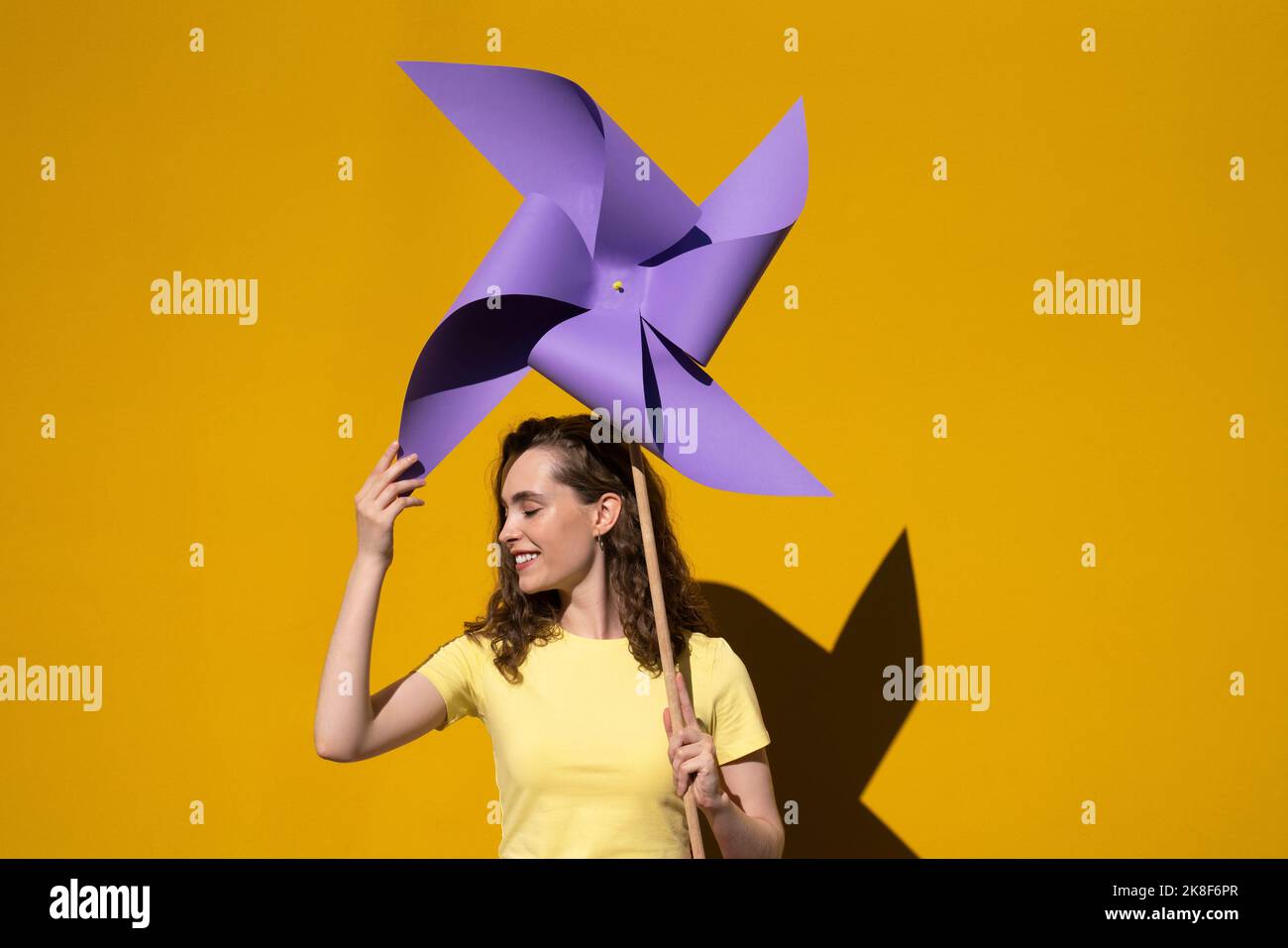 Smiling woman with eyes closed touching pinwheel toy in front of yellow ...