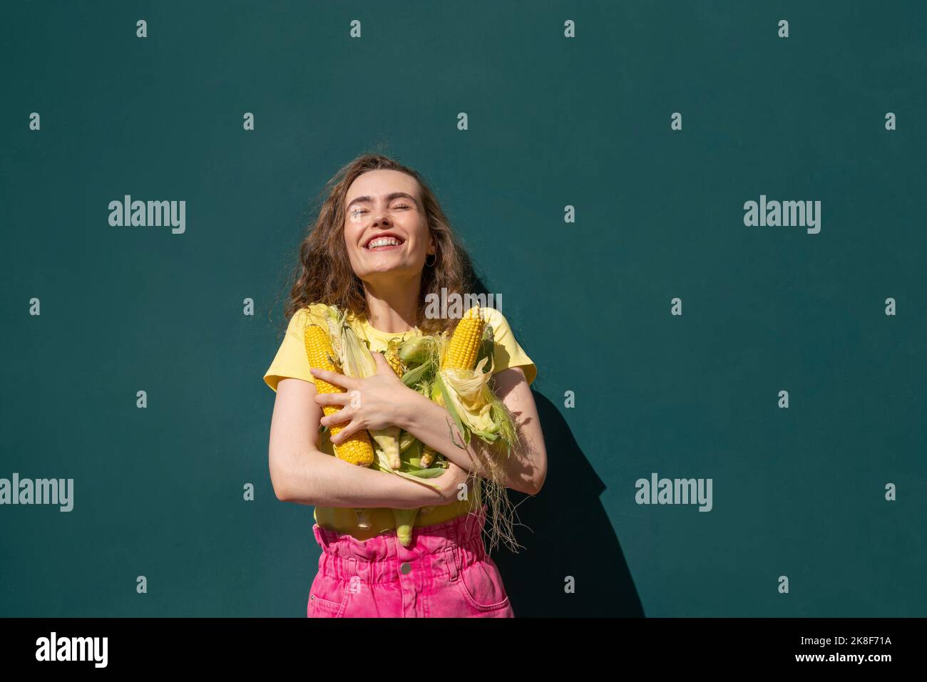 Smiling woman with eyes closed holding corns in front of wall Stock ...