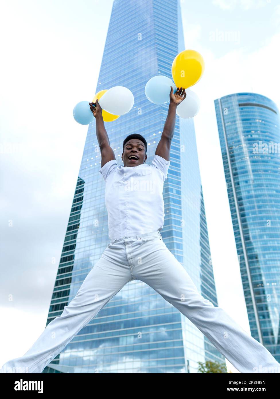 Happy man holding colorful balloon jumping in front of modern ...
