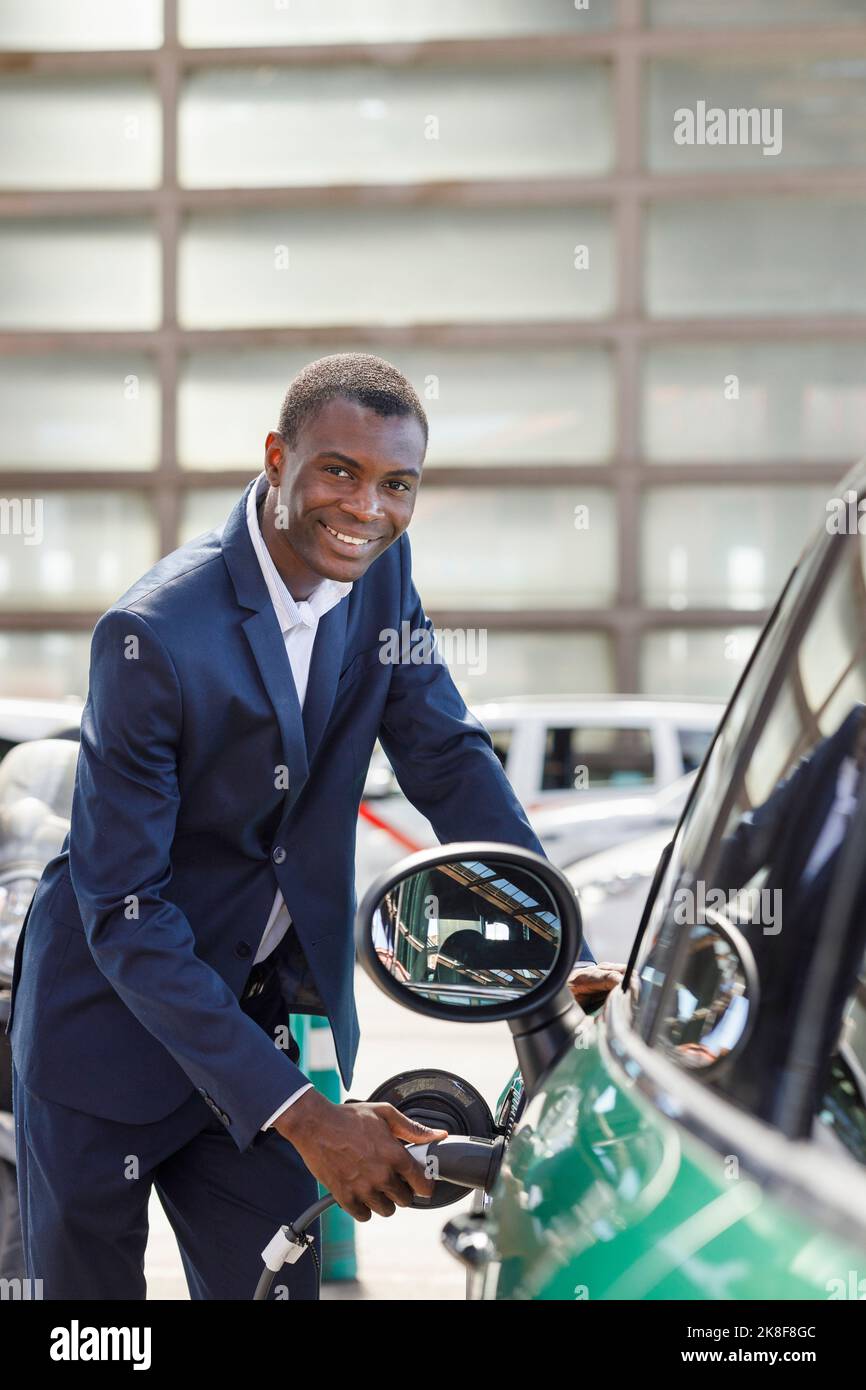 Happy businessman plugging charger in electric car at vehicle charging ...