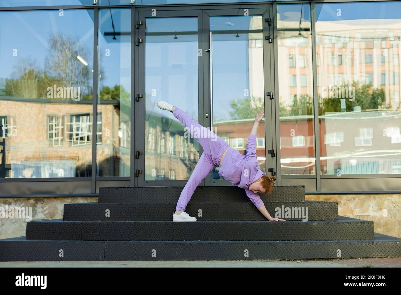 Woman doing stretching exercise on staircase in front of glass door ...