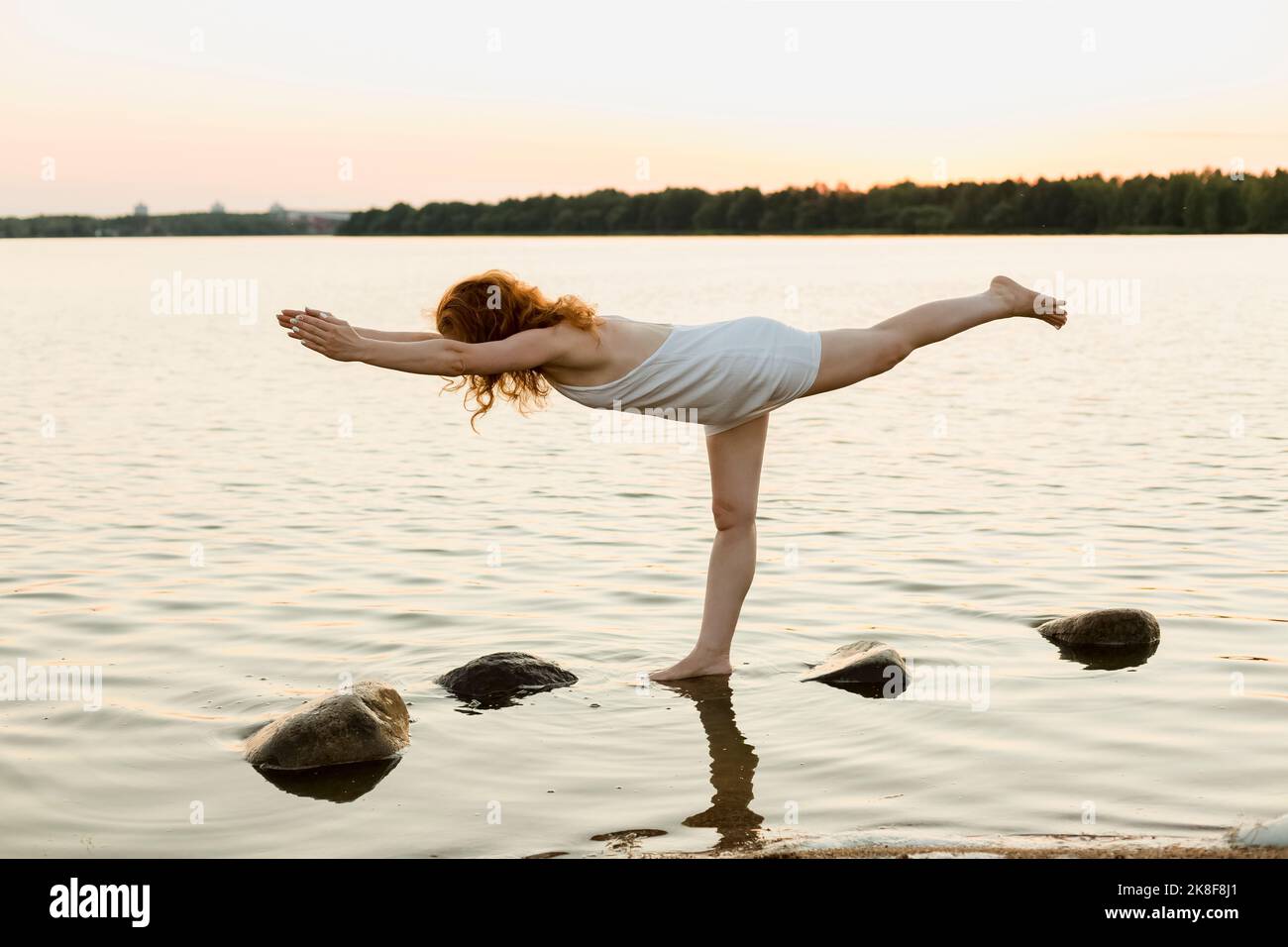 Woman practicing warrior pose amidst rocks in lake Stock Photo - Alamy