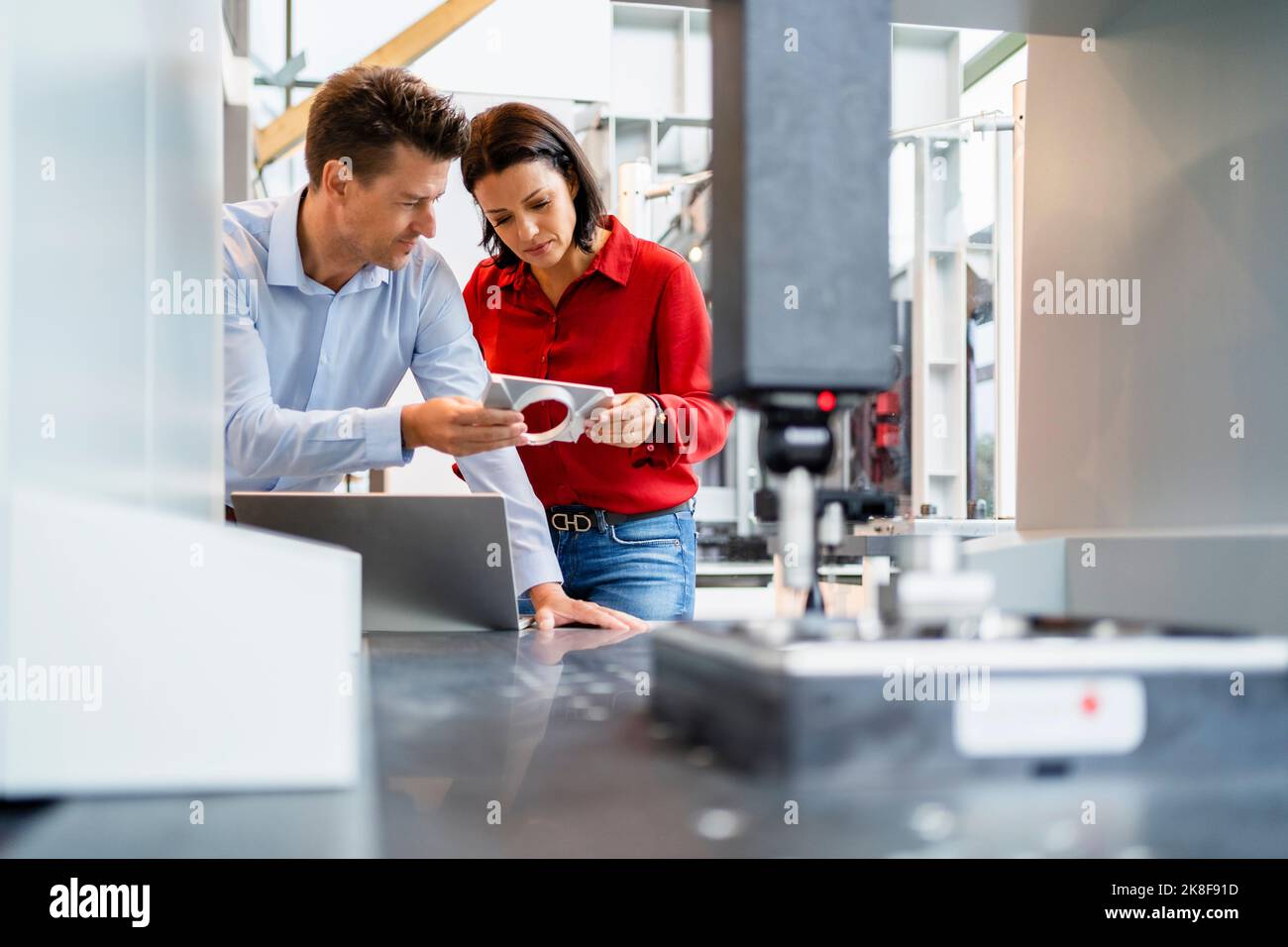 Colleagues examining machine part at factory Stock Photo - Alamy