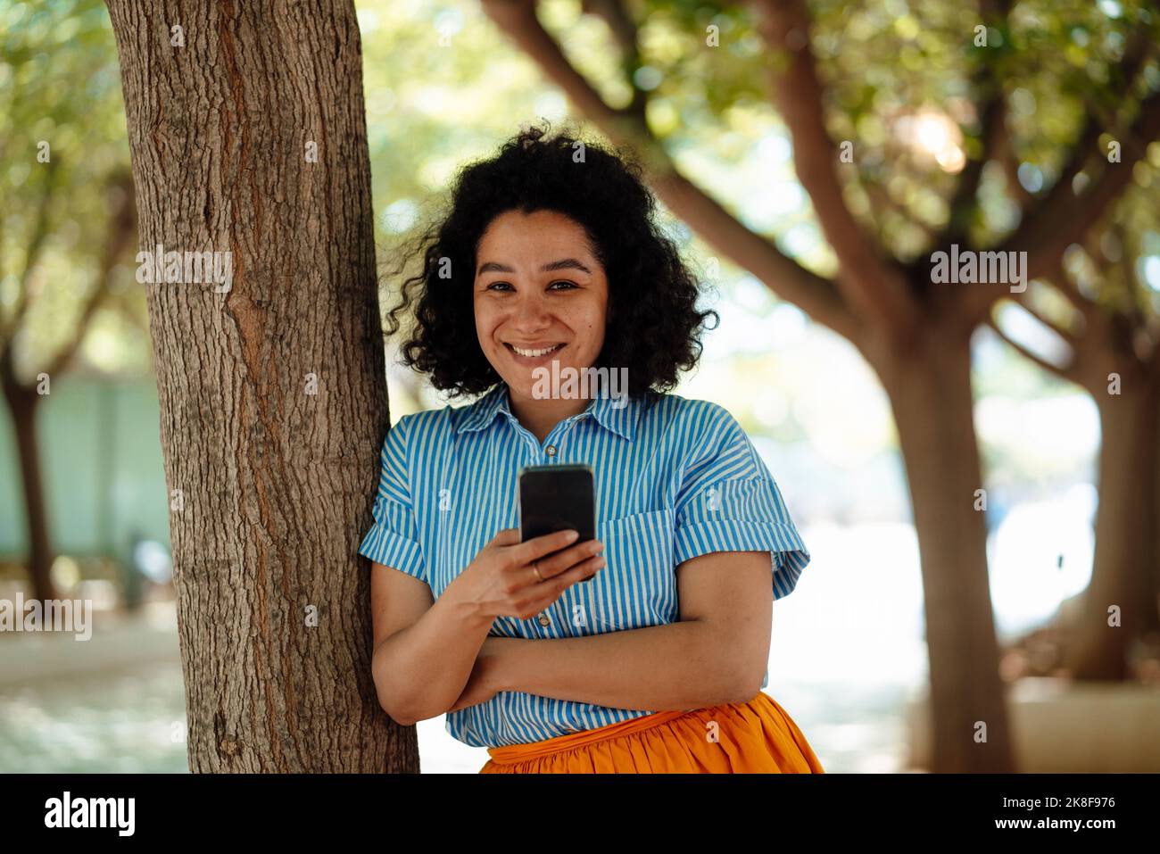 Happy woman with mobile phone leaning on tree trunk Stock Photo - Alamy