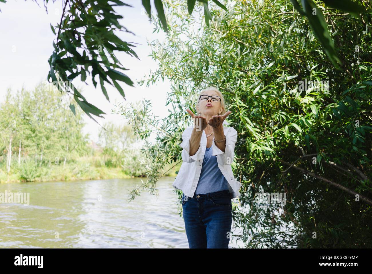 Senior woman blowing kiss standing near plants Stock Photo - Alamy