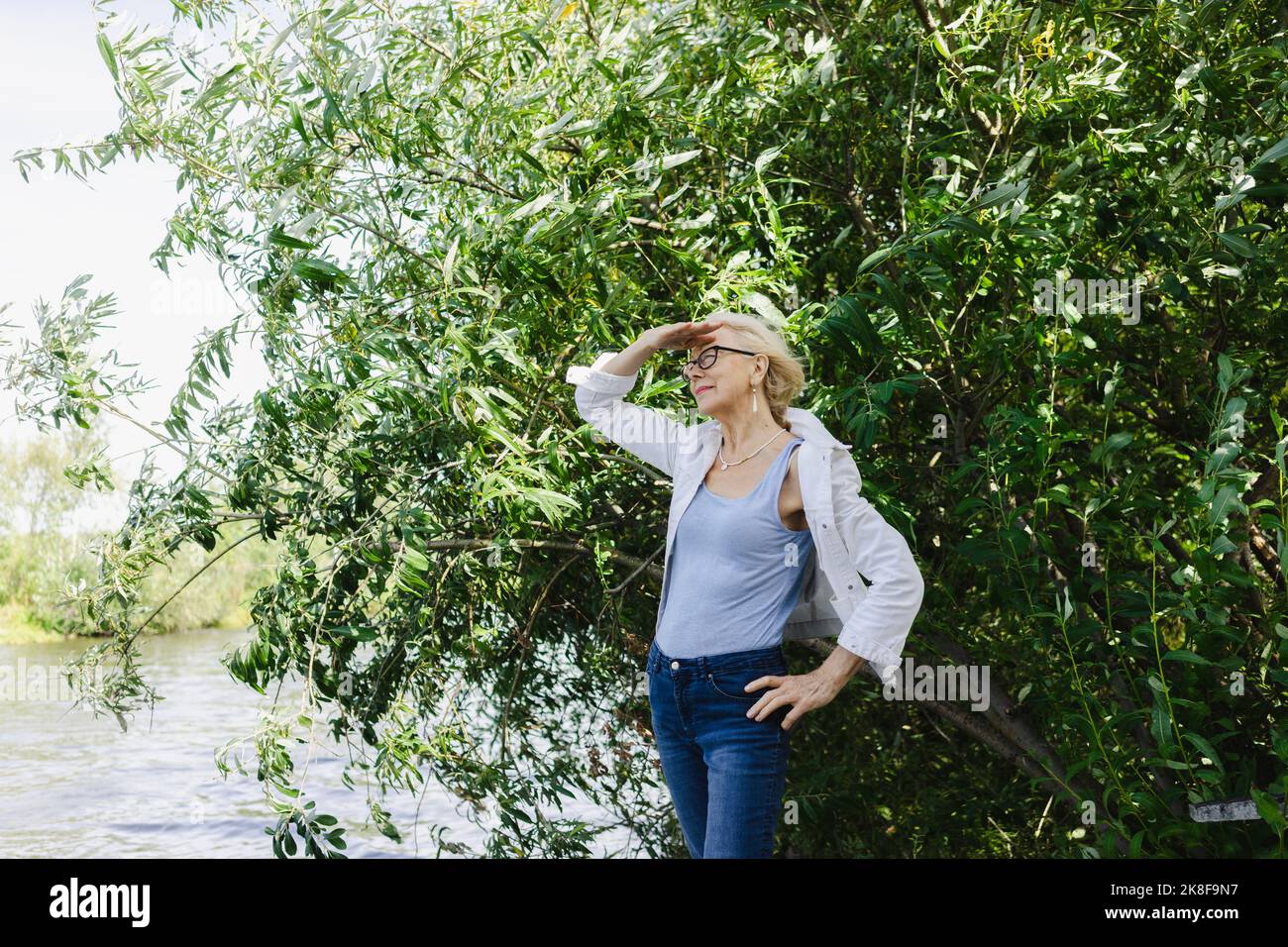Woman with hand on hip shielding eyes in front of plants Stock Photo ...