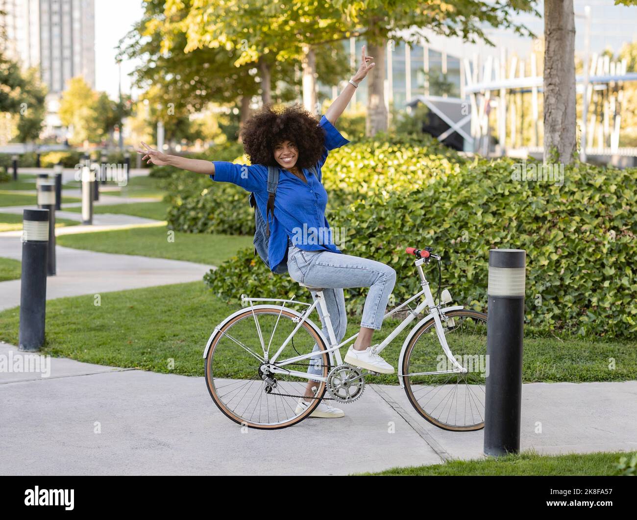 Happy Afro woman with arms raised sitting on bicycle at park Stock ...
