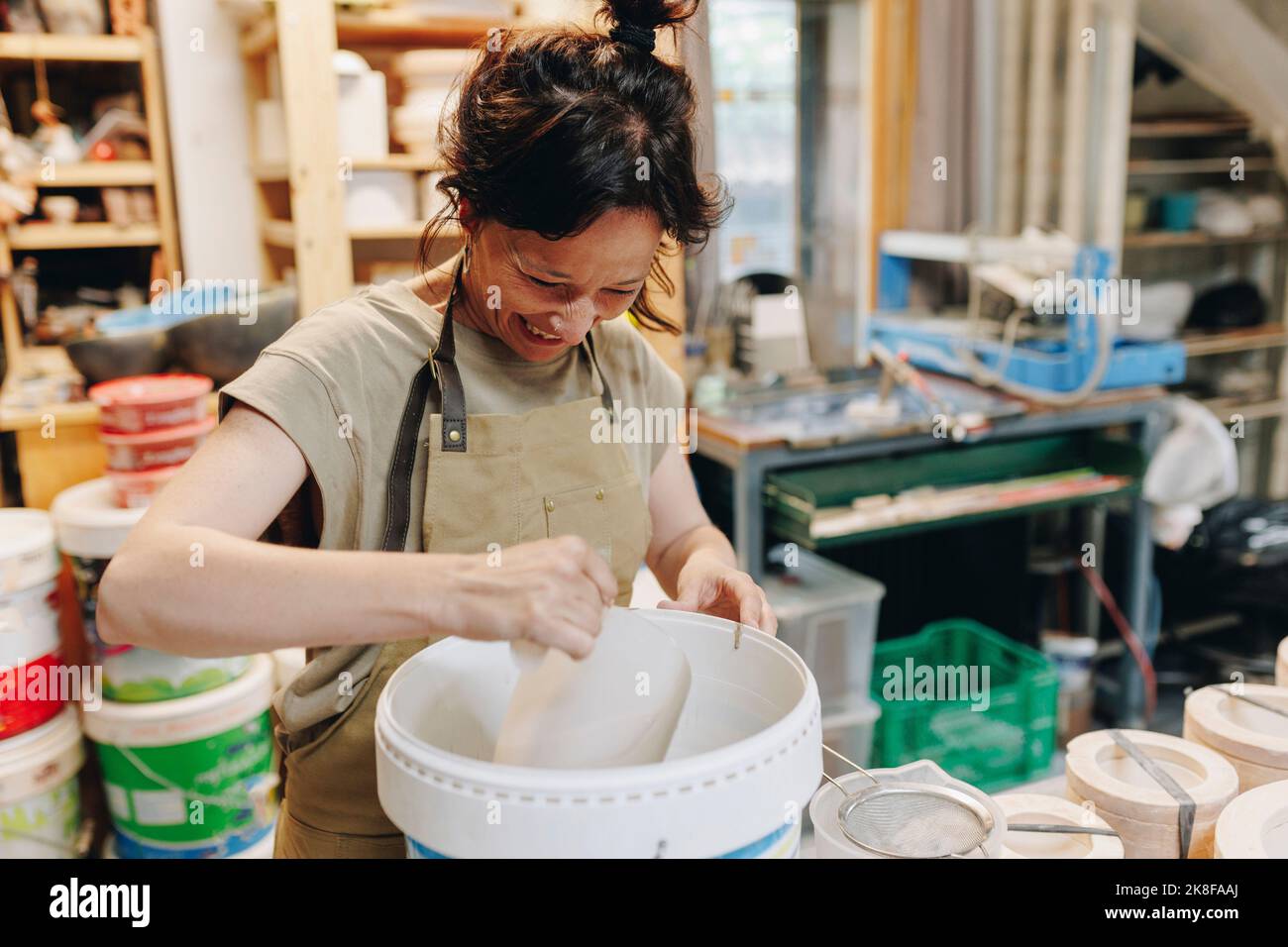 Cheerful potter with bucket of clay working at ceramics workshop Stock ...
