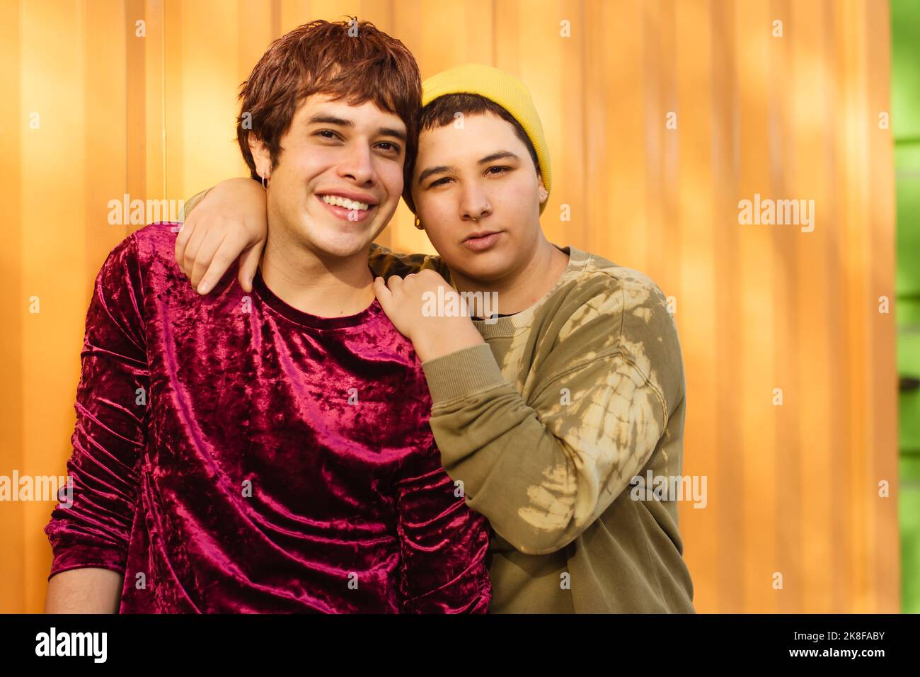 Happy non-binary couple standing in front of yellow corrugated wall ...