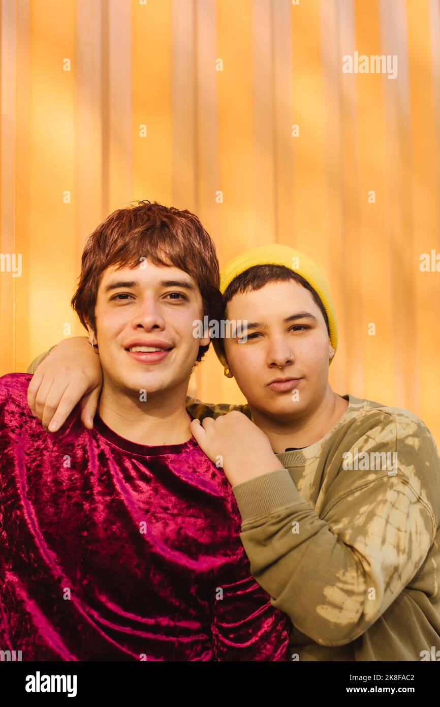 Happy non-binary couple standing together in front of yellow corrugated ...