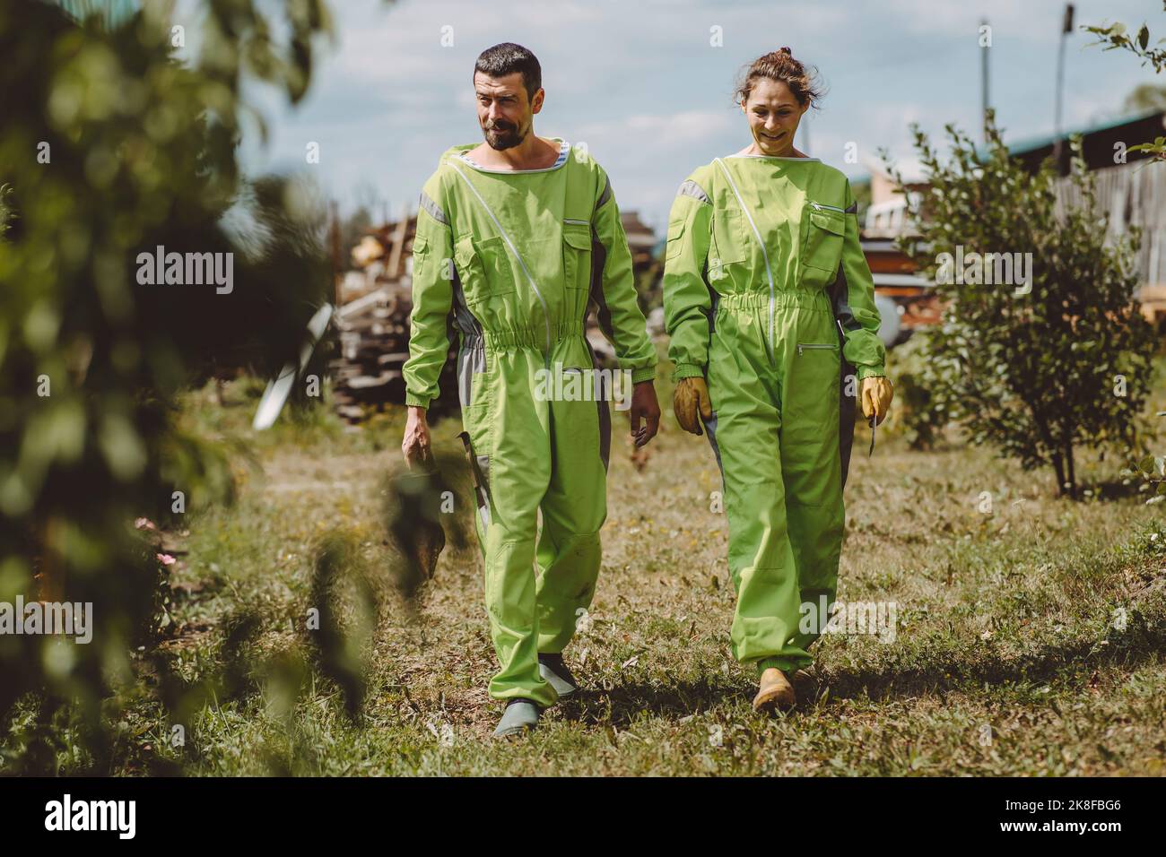 Happy beekeepers wearing protective suits walking together on apiary ...