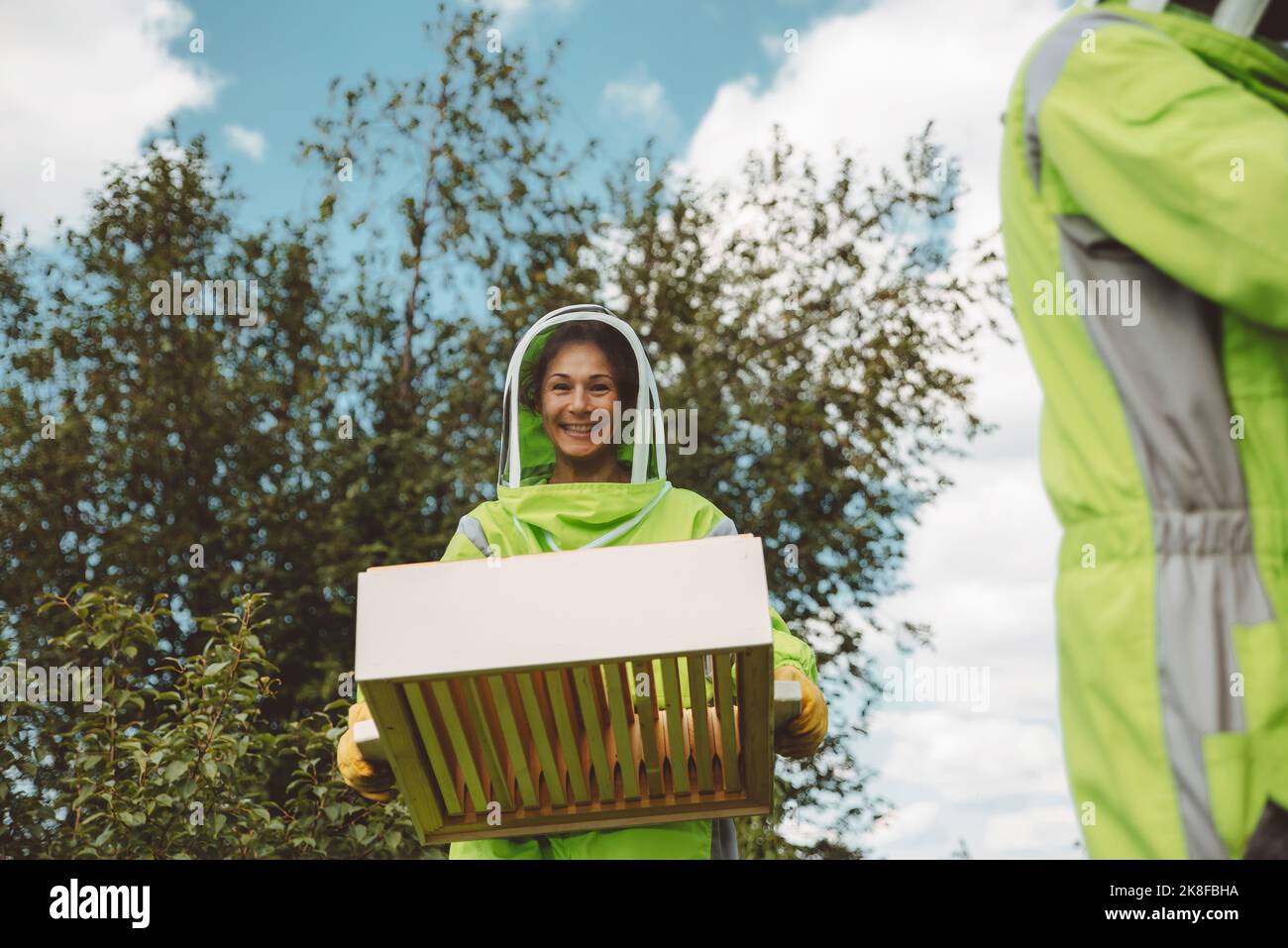 Smiling beekeeper holding beehive container in front of tree Stock ...