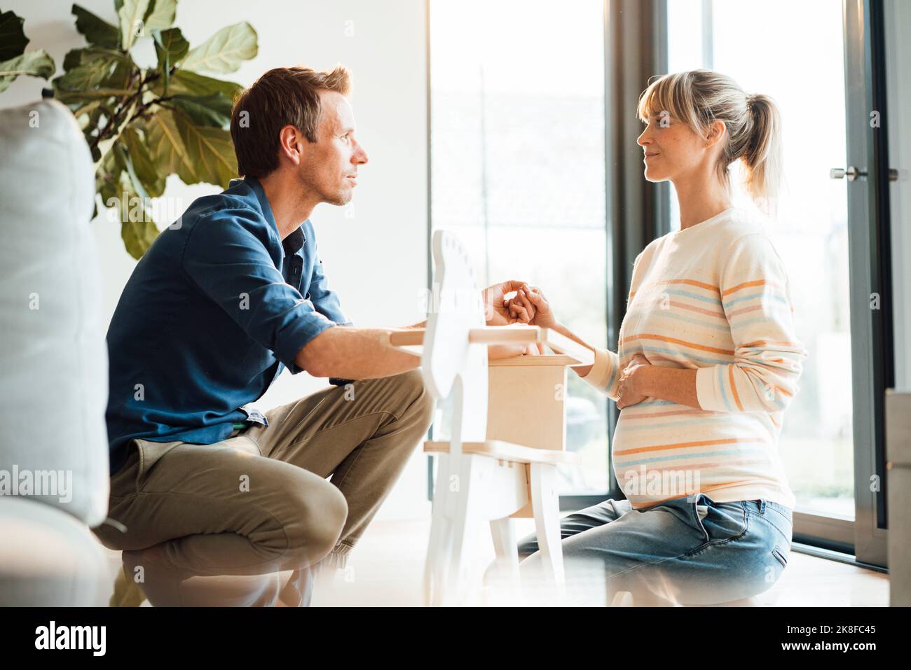 Romantic man holding hand of pregnant woman crouching near rocking ...