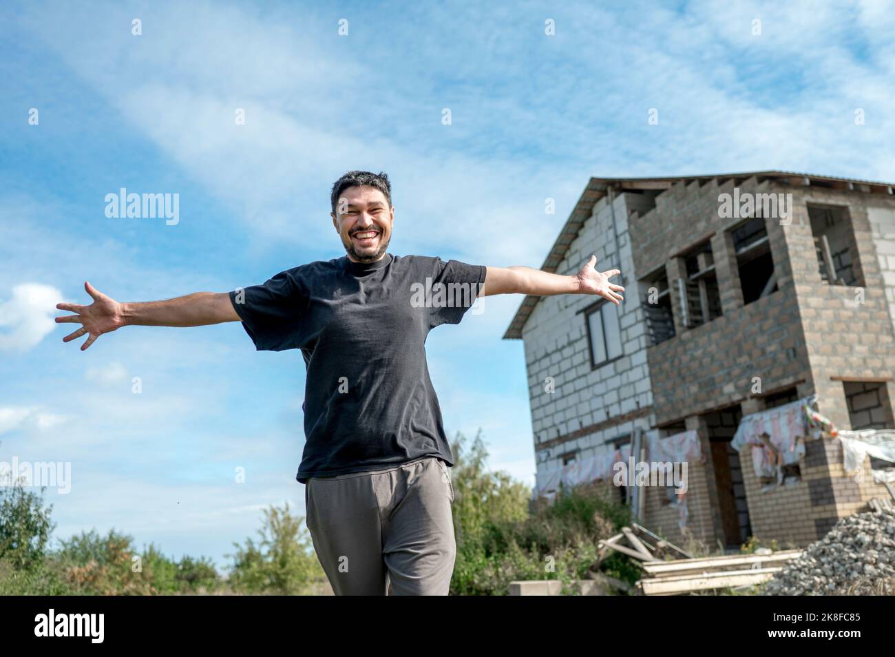 Happy man standing with arms outstretched in front of new hose under ...