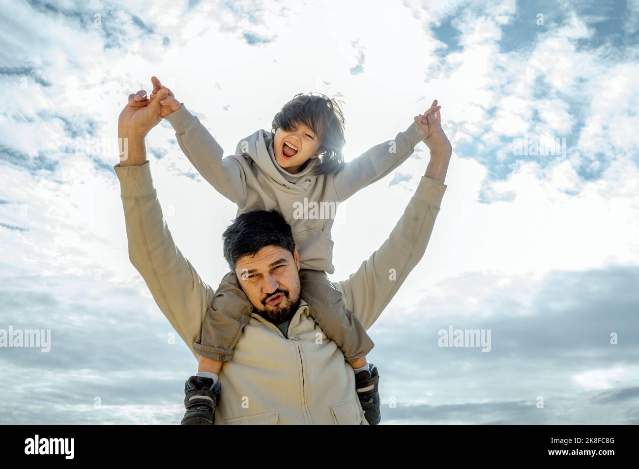 Happy son having fun sitting on father's shoulder in front of cloudy ...