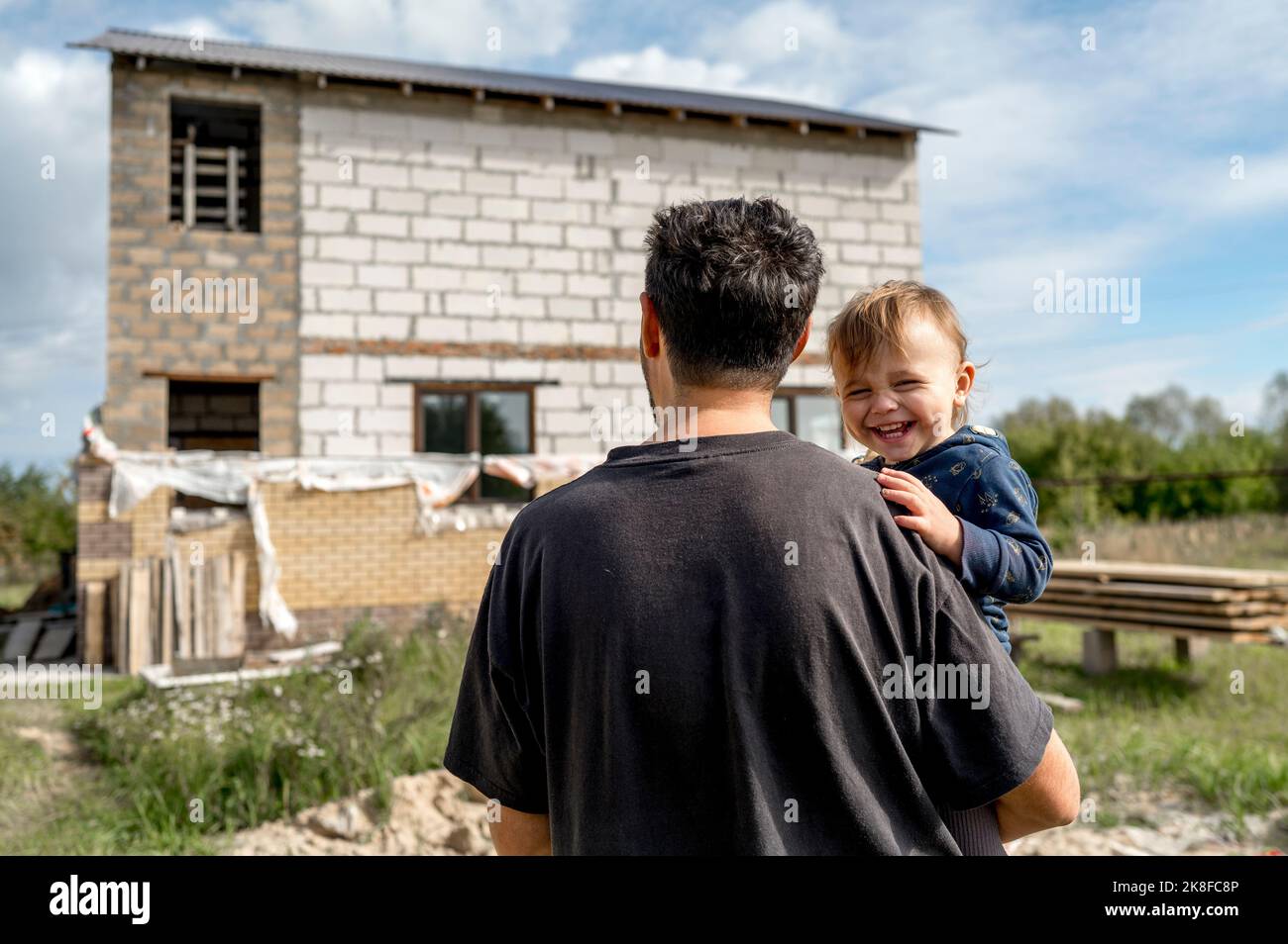 Father and cute son standing in front of house at construction site ...