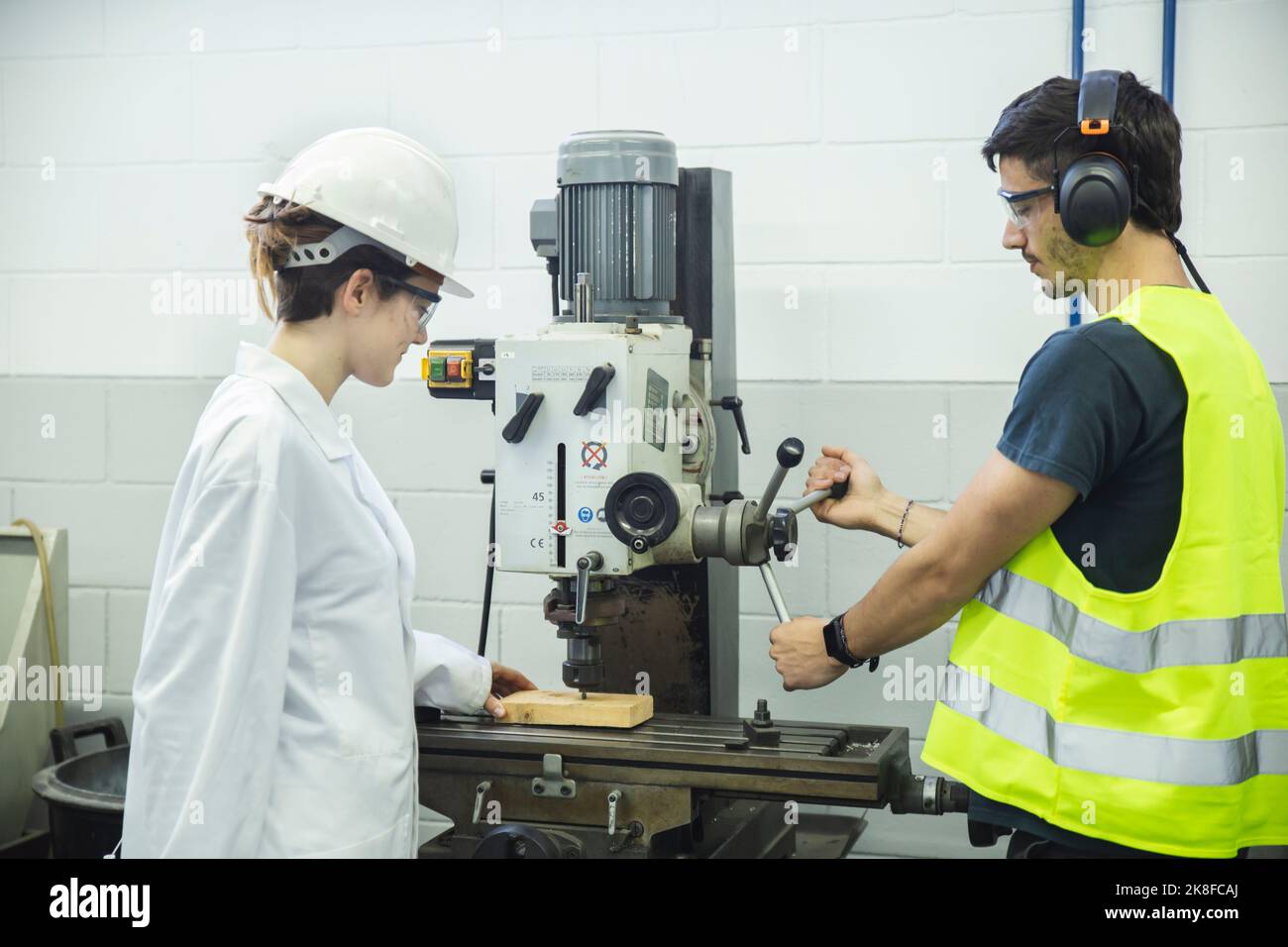 Engineer holding wood under machine by colleague working in factory ...