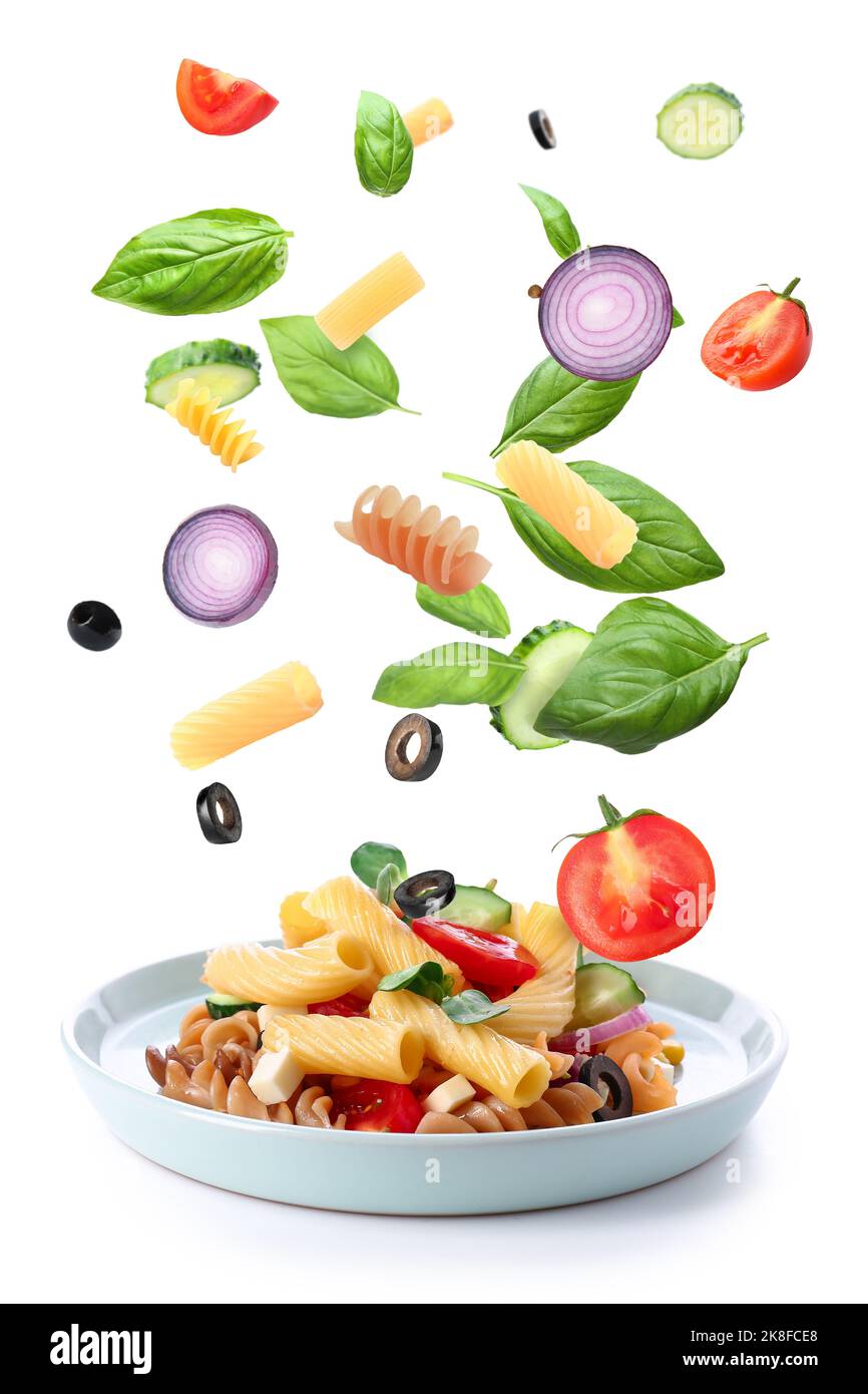 Plate with tasty pasta salad and falling ingredients on white ...
