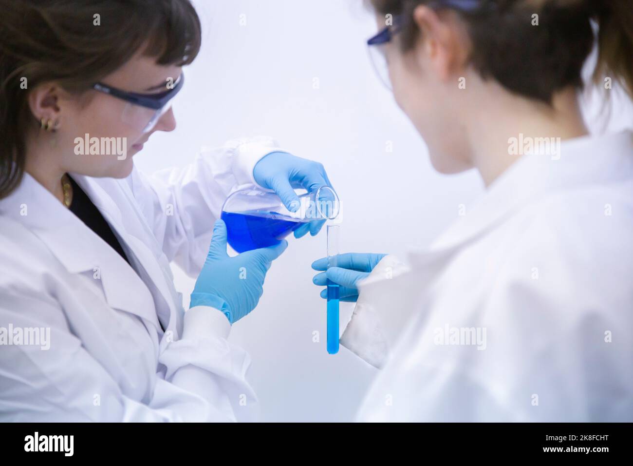 Scientist pouring chemical in test tube for experimenting by coworker ...