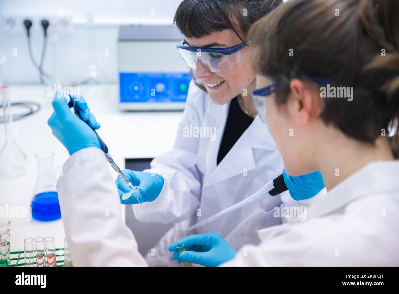 Smiling scientist using pipette for experimenting with coworker in ...
