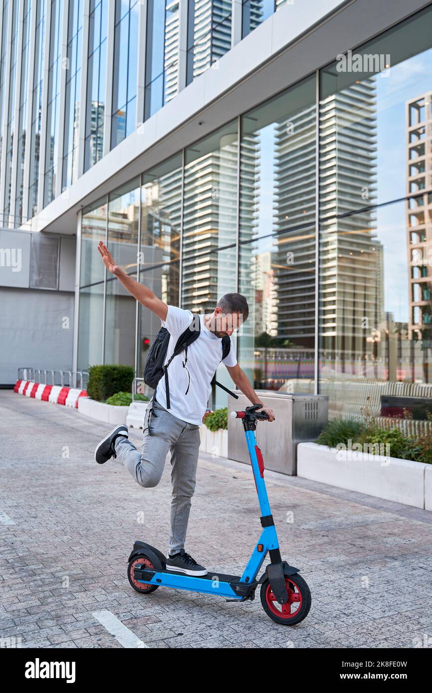 Man with hand raised balancing on electric push scooter in front of ...