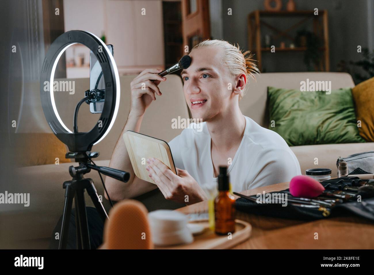 Smiling influencer filming make-up tutorial through smart phone at home ...