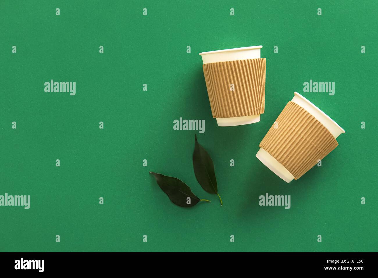 Paper cups and plant leaves on green background Stock Photo - Alamy
