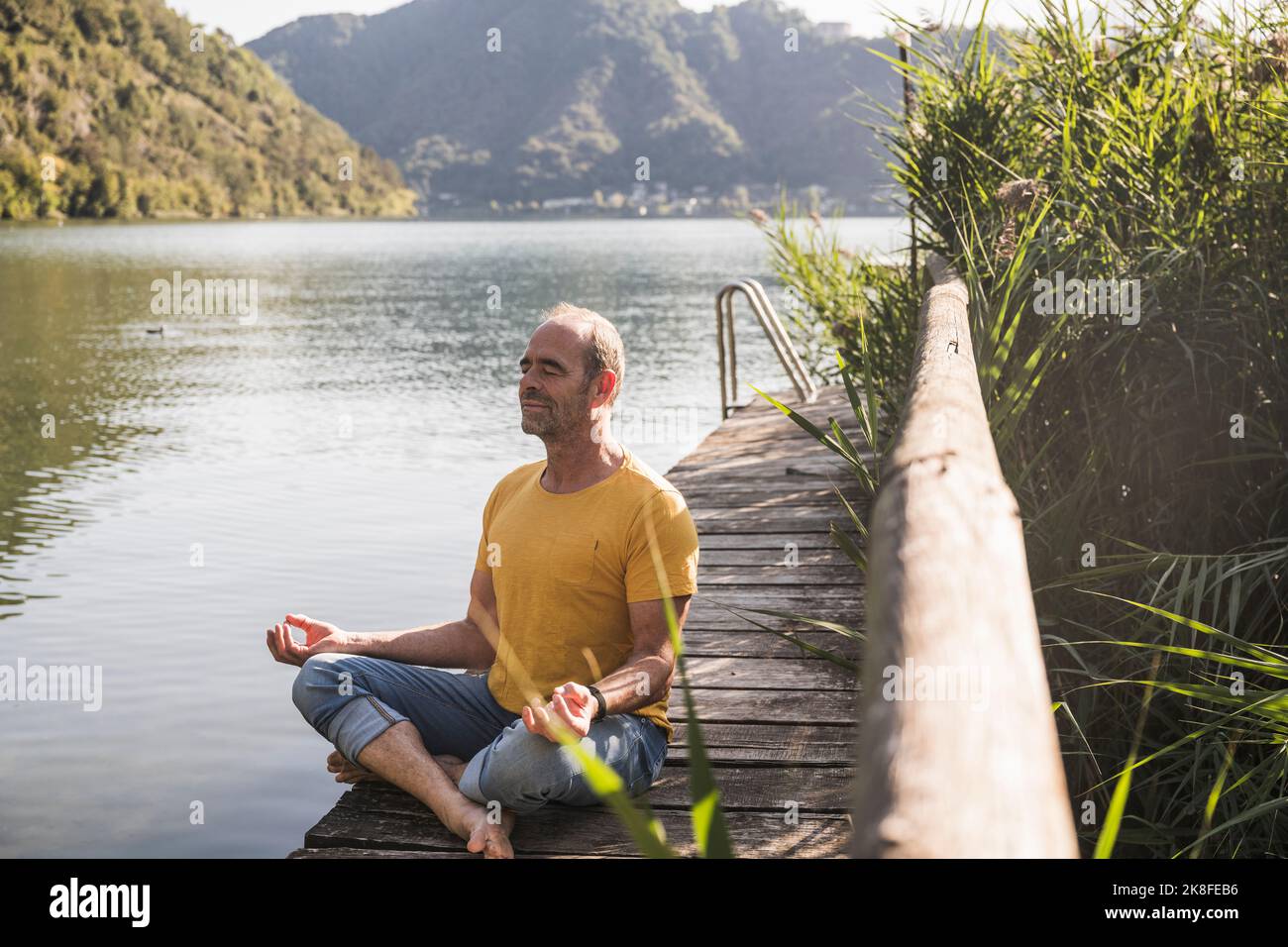 Mature man practicing lotus position on jetty by lake Stock Photo - Alamy