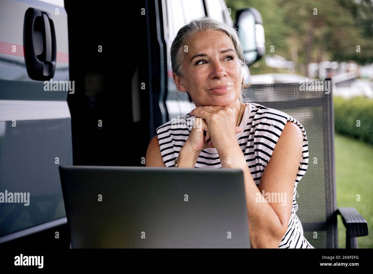 Contemplative freelancer sitting with hand on chin outside camper van ...