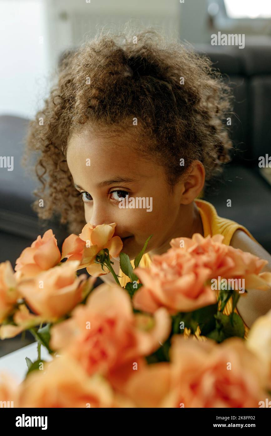 Smiling girl smelling orange roses at home Stock Photo - Alamy