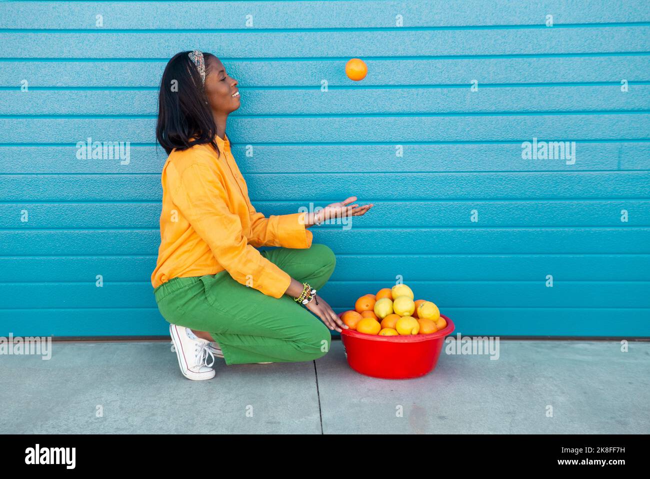 Young woman juggling with oranges in front of blue roller shutter Stock ...