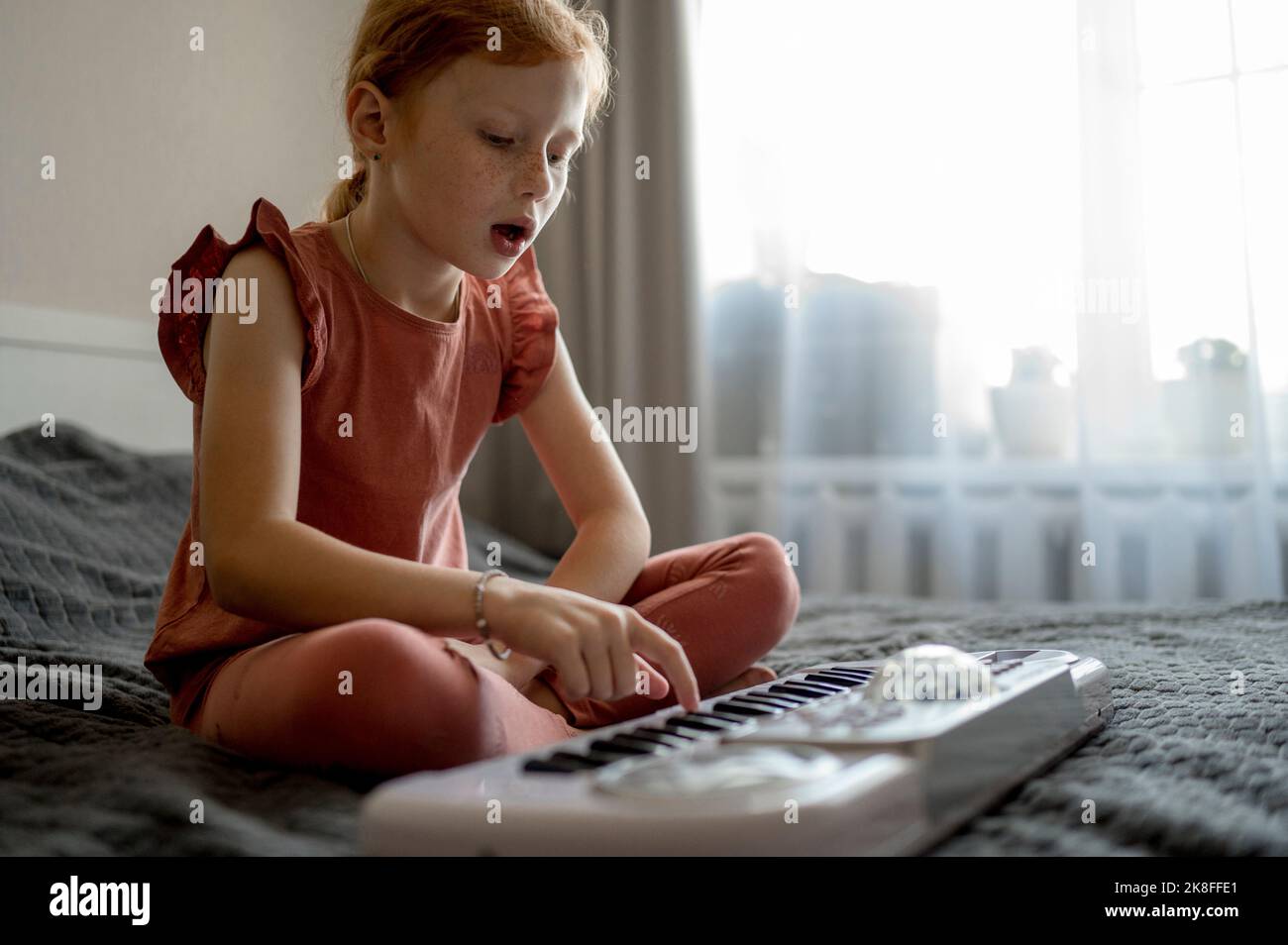 Girl singing and practicing synthesizer on bed at home Stock Photo - Alamy