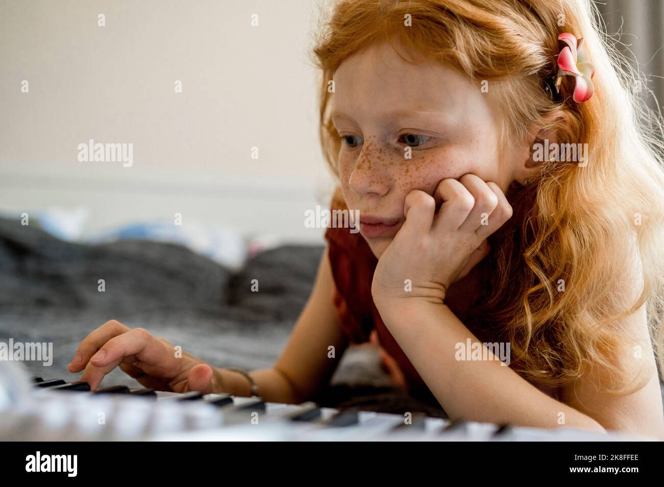 Girl with red hair playing synthesizer lying on bed Stock Photo - Alamy