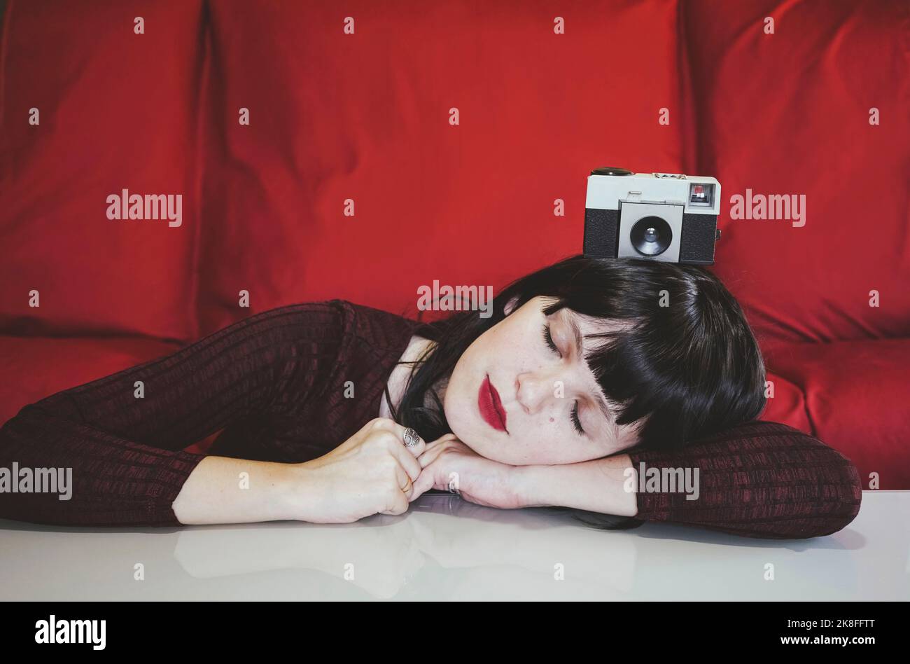 Woman resting on table with analog camera in front of red couch Stock ...