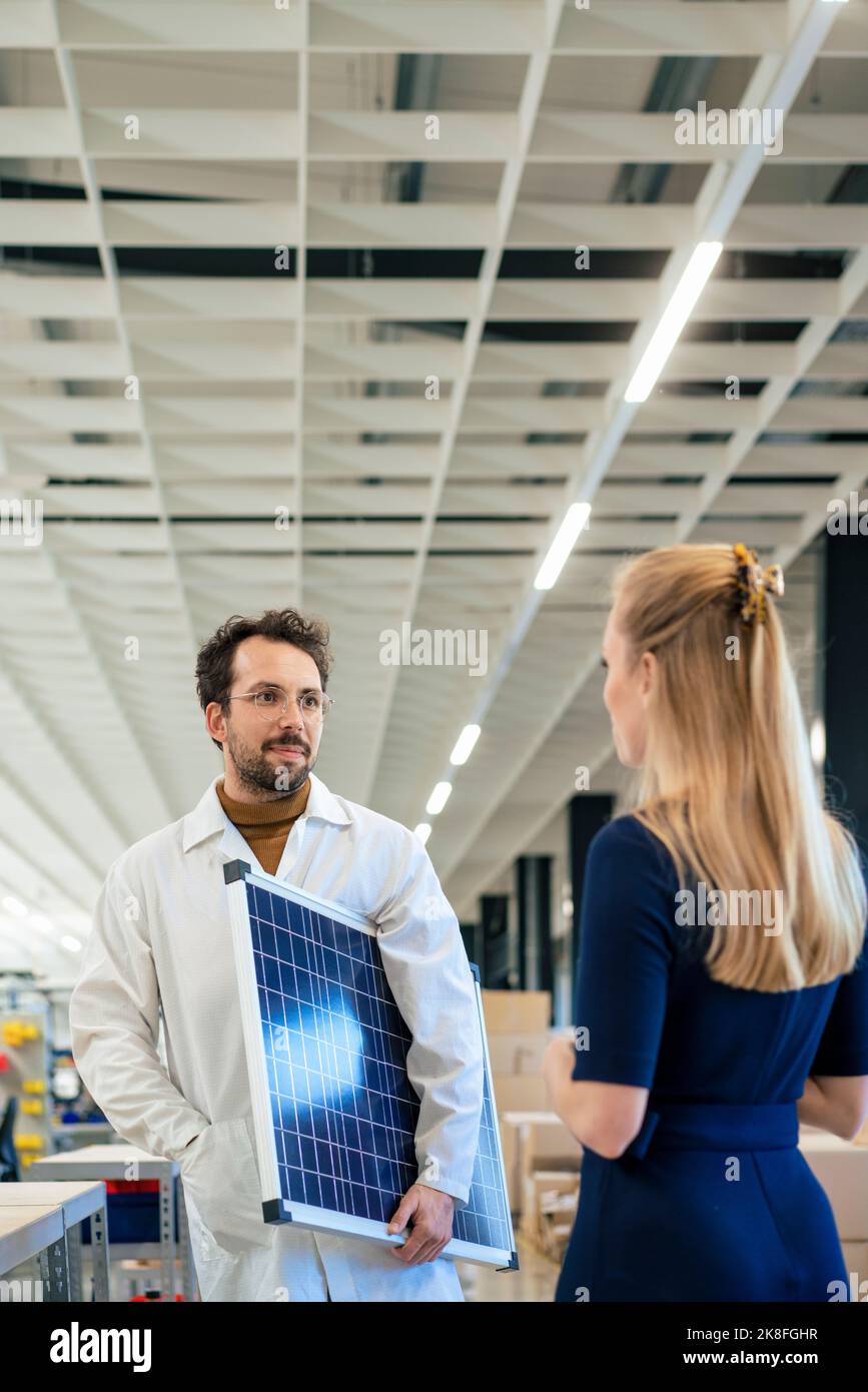 Engineer holding solar panel talking to colleague in industry Stock ...