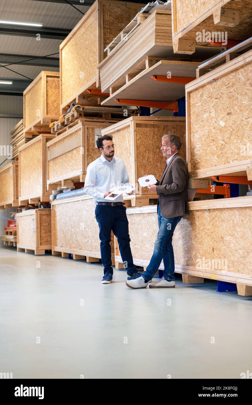 Senior businessman with colleague standing by storage compartment at ...