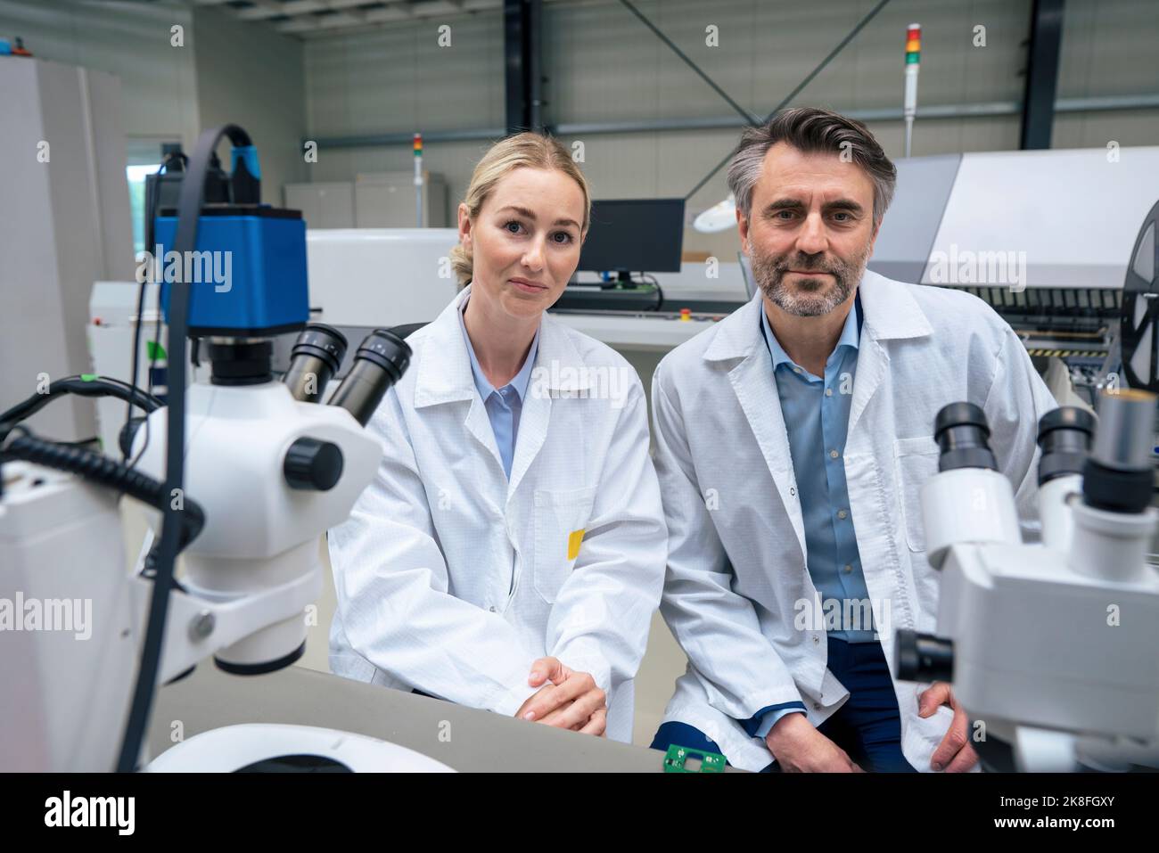 Smiling scientists wearing lab coat sitting in industry Stock Photo - Alamy
