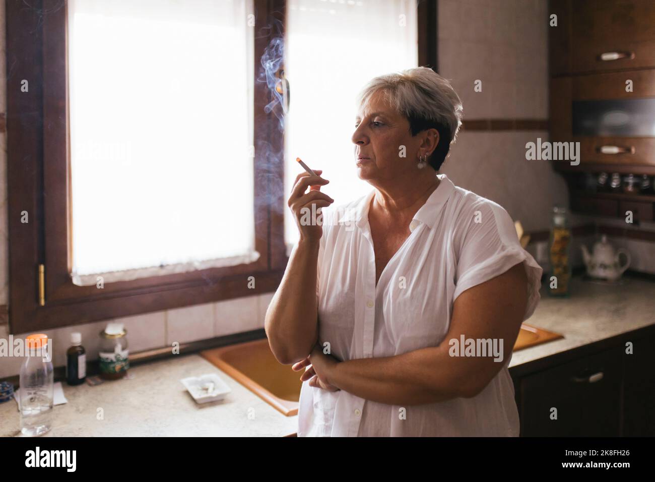 Depressed woman smoking cigarette in kitchen at home Stock Photo - Alamy