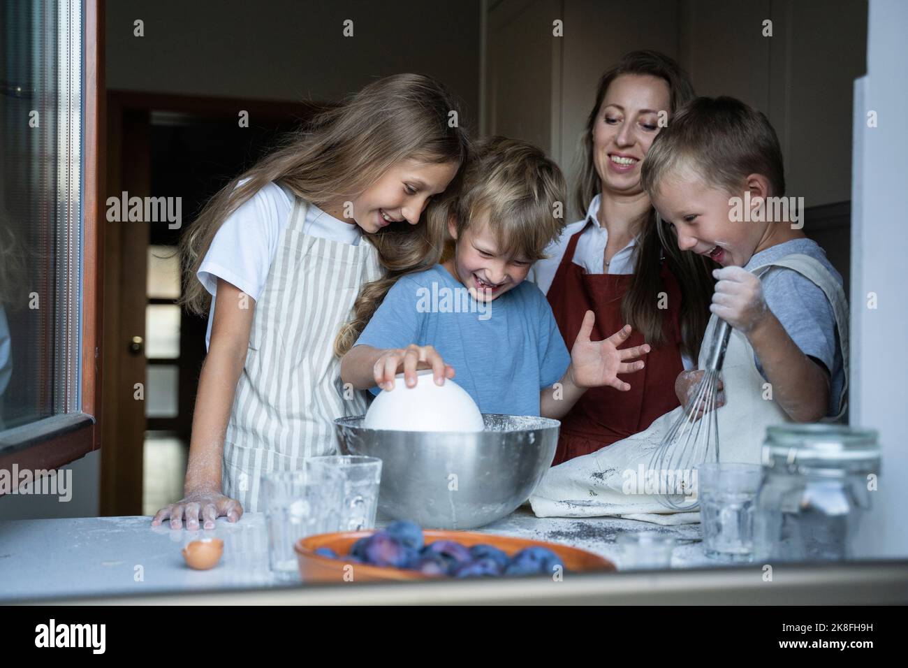 Happy children preparing batter by mother in kitchen at home Stock ...