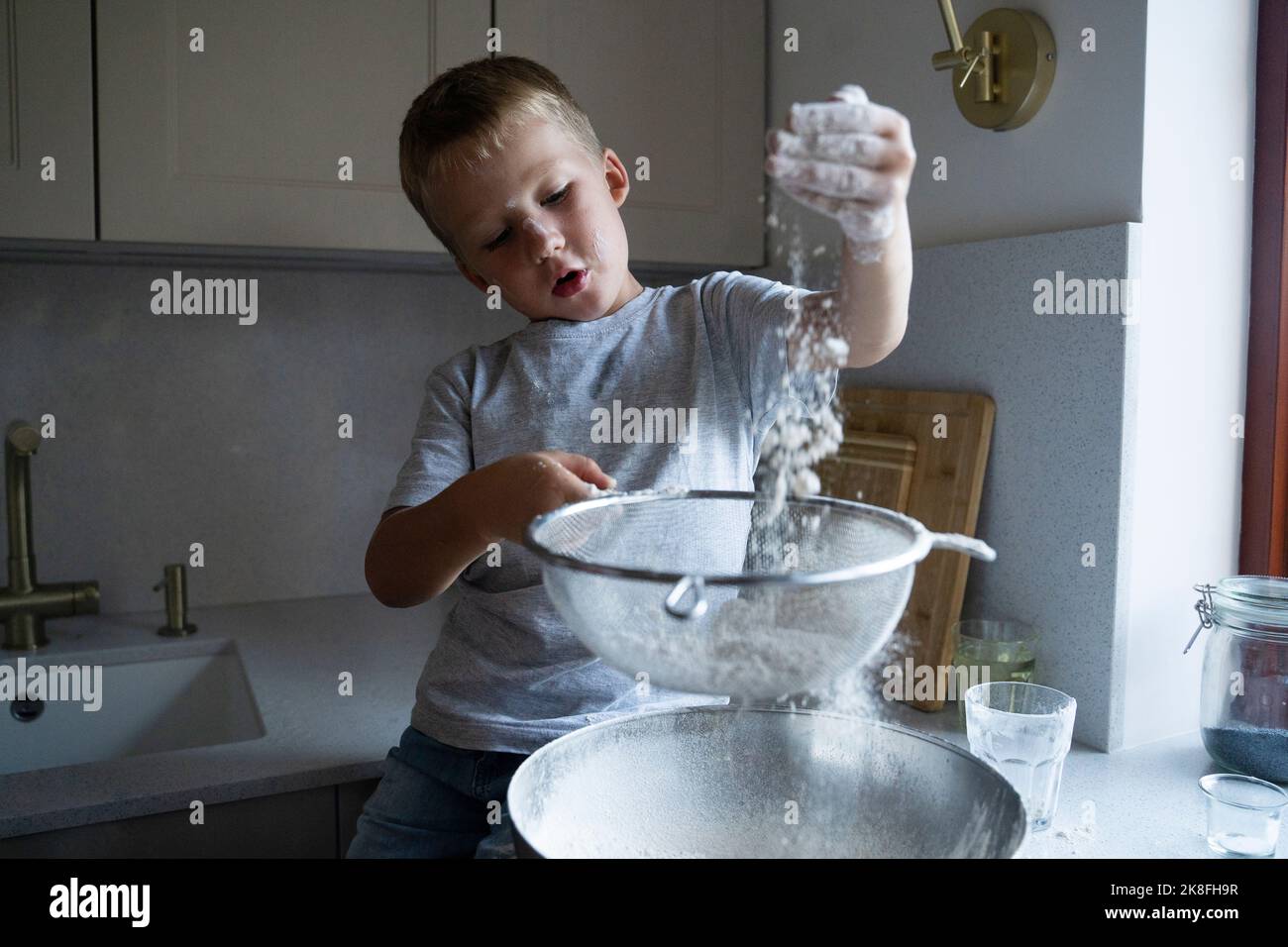 Cute boy sieving flour for cake preparation at home Stock Photo - Alamy