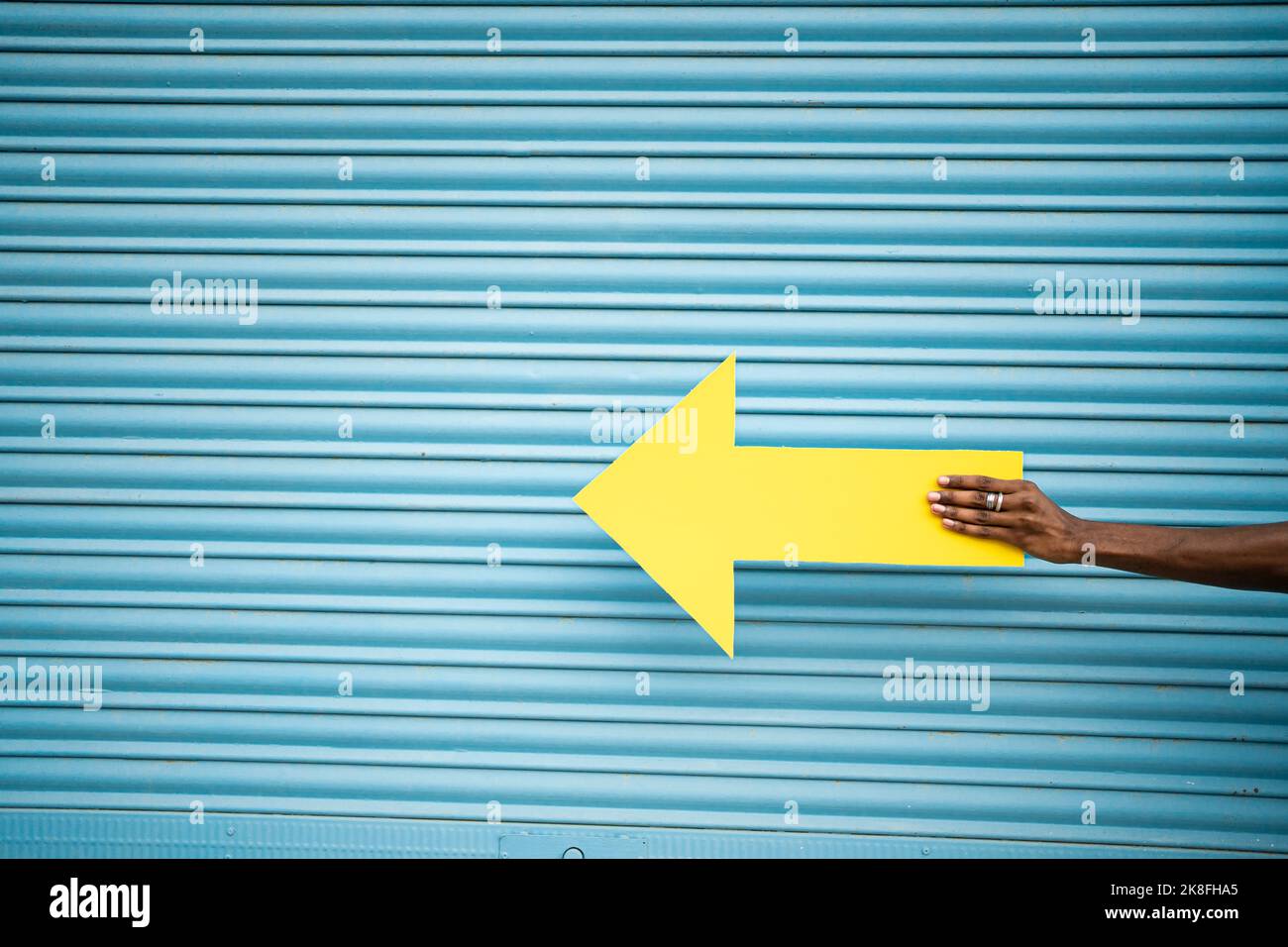 Hand of man holding yellow arrow sign in front of blue shutter Stock ...