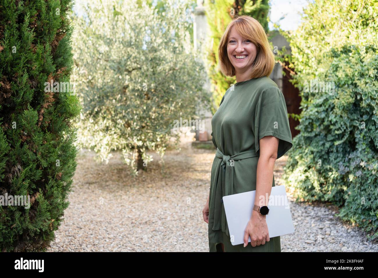 Happy freelancer standing with laptop in garden Stock Photo - Alamy