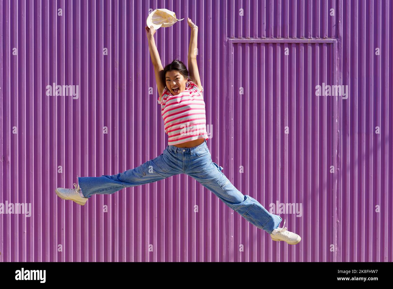 Happy woman jumping in front of purple wall Stock Photo - Alamy
