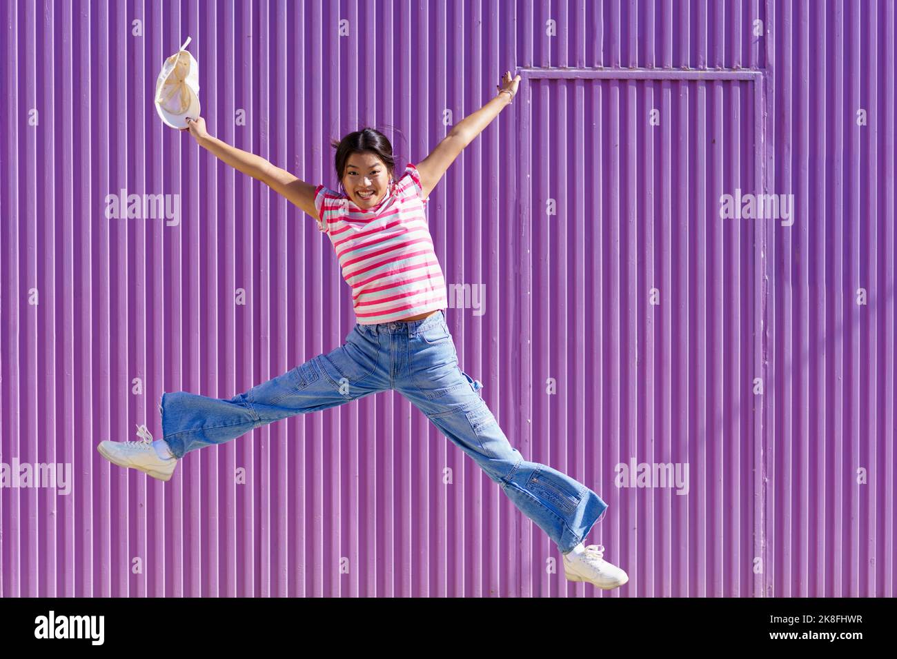 Happy young woman jumping in front of purple background Stock Photo - Alamy